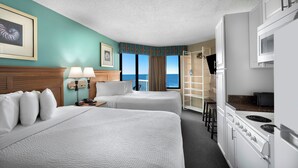 Quarto de hotel com duas camas, uma kitchenette, uma televisão e vista para o oceano.