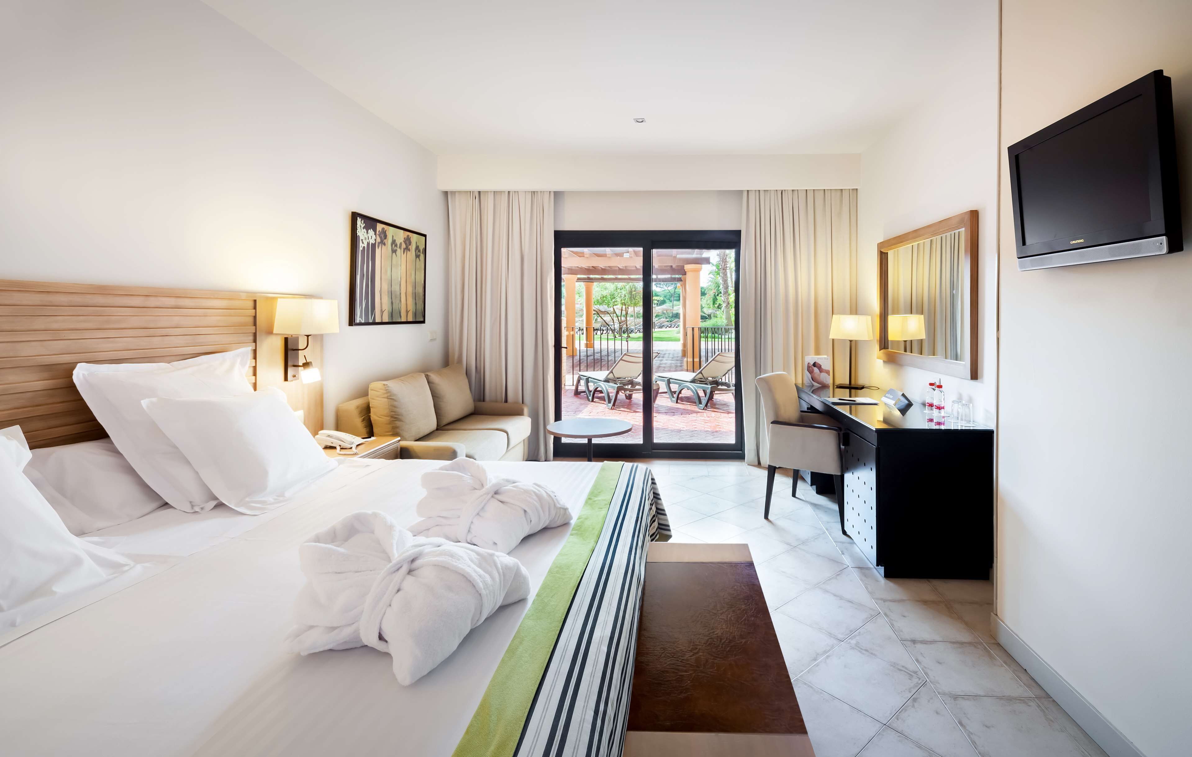 Quarto de hotel com cama, escrivaninha, cadeira, televisão e vista para a área externa.