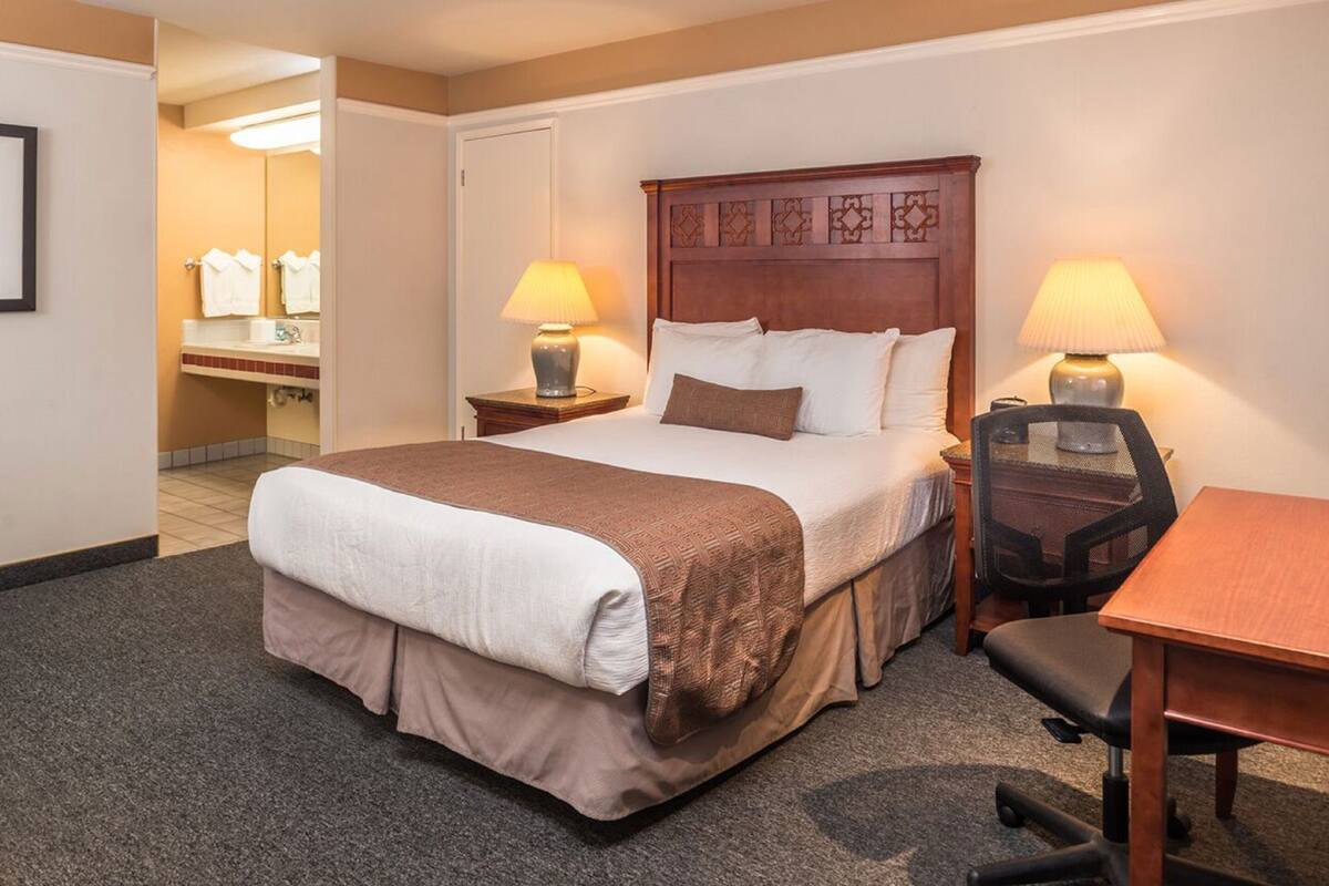 Quarto de hotel com uma cama grande, duas mesas de cabeceira com abajures, uma escrivaninha e uma cadeira.