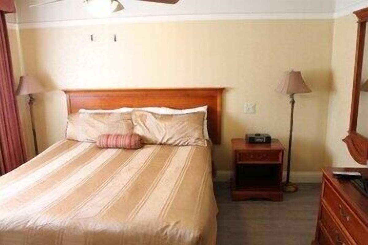 Quarto de hotel com cama, mesas de cabeceira, luminária e cômoda.