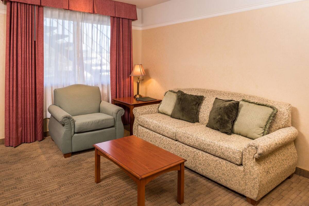 Uma sala de estar com uma poltrona verde, um sofá estampado e uma mesa de centro de madeira.