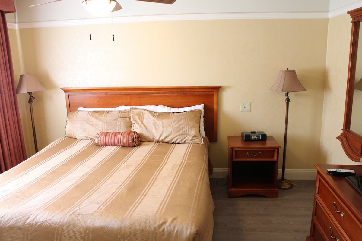 Uma cama bem arrumada com colcha listrada, cabeceira de madeira e duas luminárias de cabeceira.