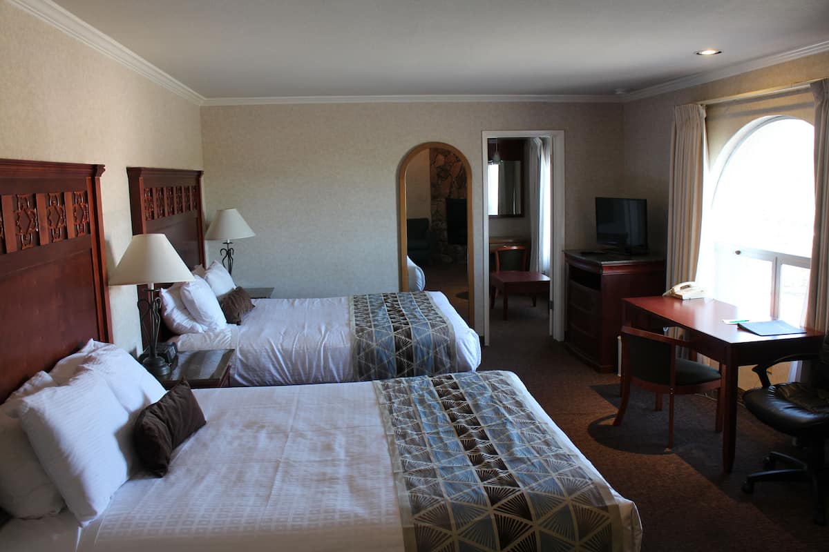 Quarto de hotel com duas camas, uma mesa, uma cadeira, uma televisão e uma janela com cortinas.