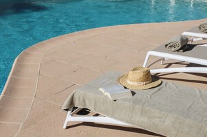 Uma área à beira da piscina com espreguiçadeiras, um guarda-sol e um chapéu de palha.