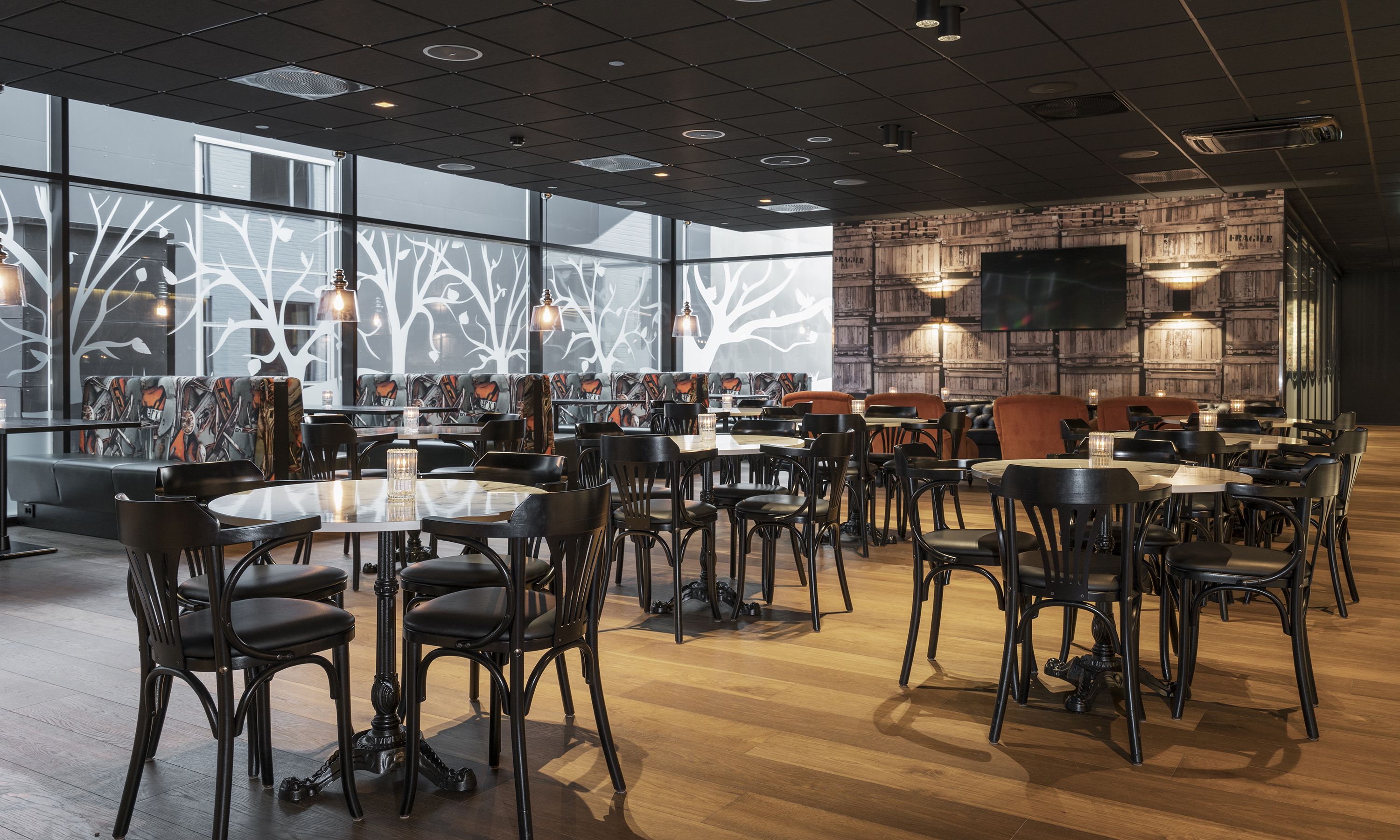 Uma sala de jantar ampla com pé direito alto, iluminação moderna e diversos tipos de assentos, incluindo mesas e cabines.