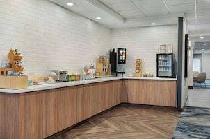 Uma área de recepção de hotel com balcão de madeira, dispensador de bebidas e geladeira.