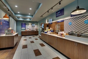 Espaço de café da manhã com balcão, variedade de alimentos para o café da manhã e parede com padrão geométrico.