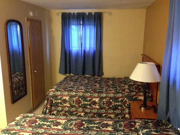 Quarto de hotel com cama, mesa de cabeceira, luminária, espelho e porta.