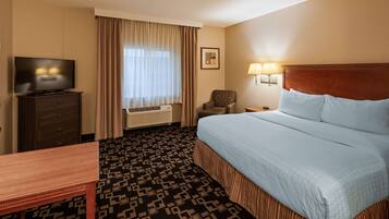 Quarto de hotel com cama, televisão, secretária, cadeira, abajur e um quadro na parede.