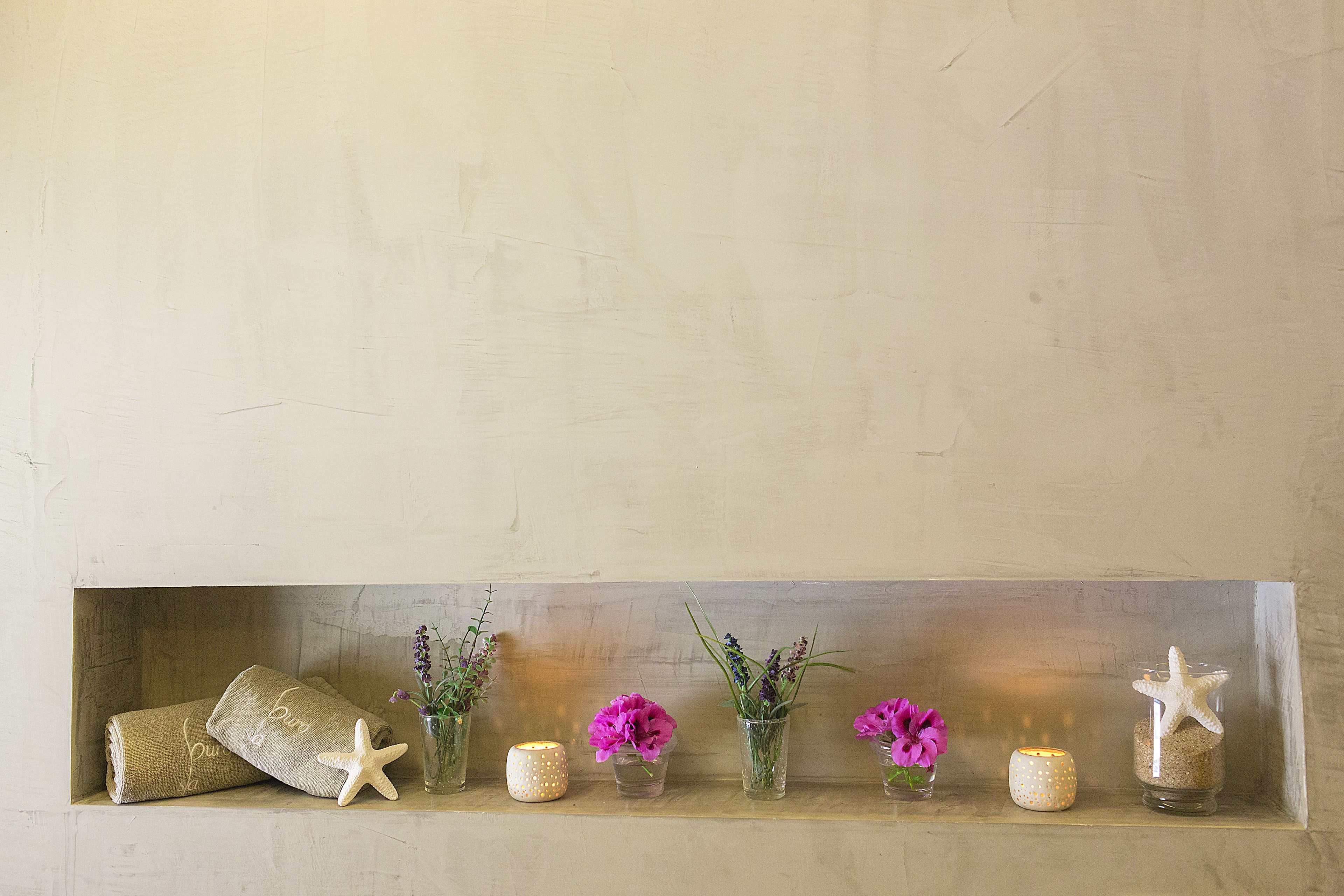 Uma prateleira com uma toalha enrolada, estrelas-do-mar e pequenos vasos com flores e velas.