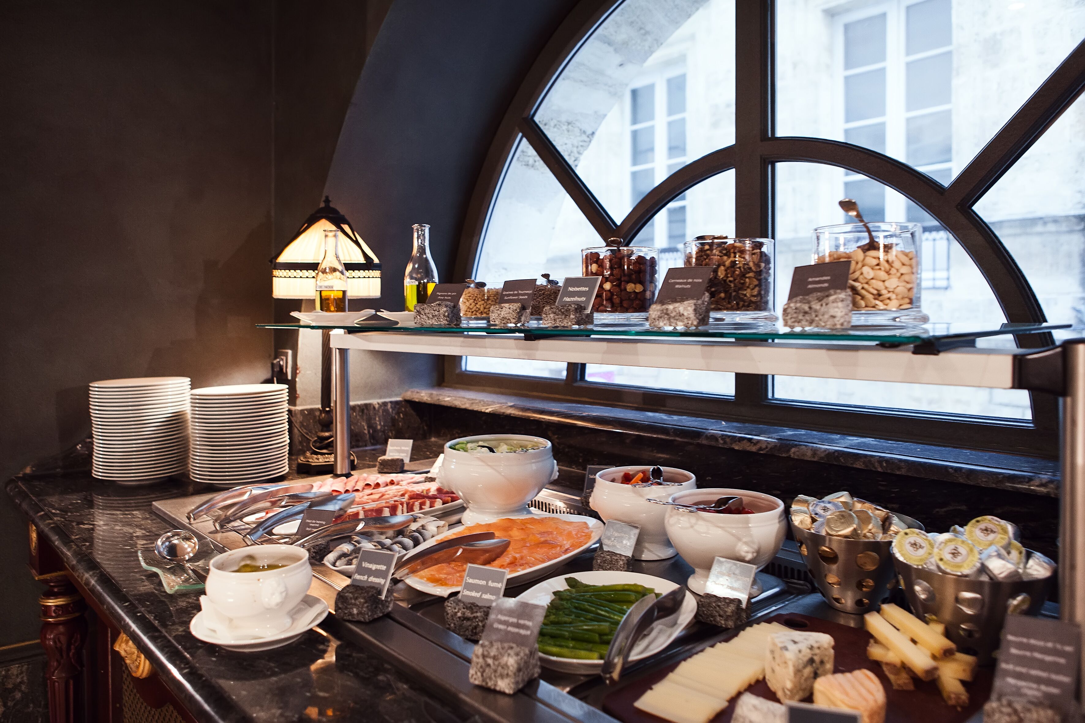Buffet com diversos alimentos e acompanhamentos, dispostos em um balcão com vista para a janela.