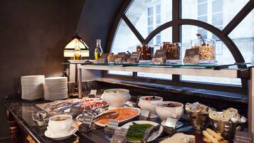 Buffet com diversos alimentos e acompanhamentos, dispostos em um balcão com vista para a janela.