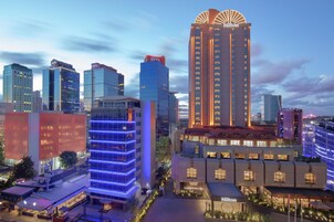 Paisagem urbana com um hotel Hilton em destaque, edifícios modernos e sinalização iluminada.