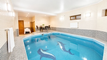 Uma piscina com arte em azulejos de golfinhos, um espaço iluminado pelo sol com mesa e cadeiras, e uma parede revestida em azulejos.