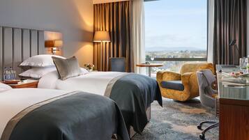 Quarto de hotel com duas camas, uma escrivaninha, uma cadeira e vista para a cidade.