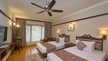 Quarto de hotel com duas camas, um ventilador de teto, escrivaninha com cadeira, televisão e janela com cortinas.