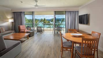 Quarto de hotel moderno com varanda, sofá, mesa de jantar e televisão na parede.