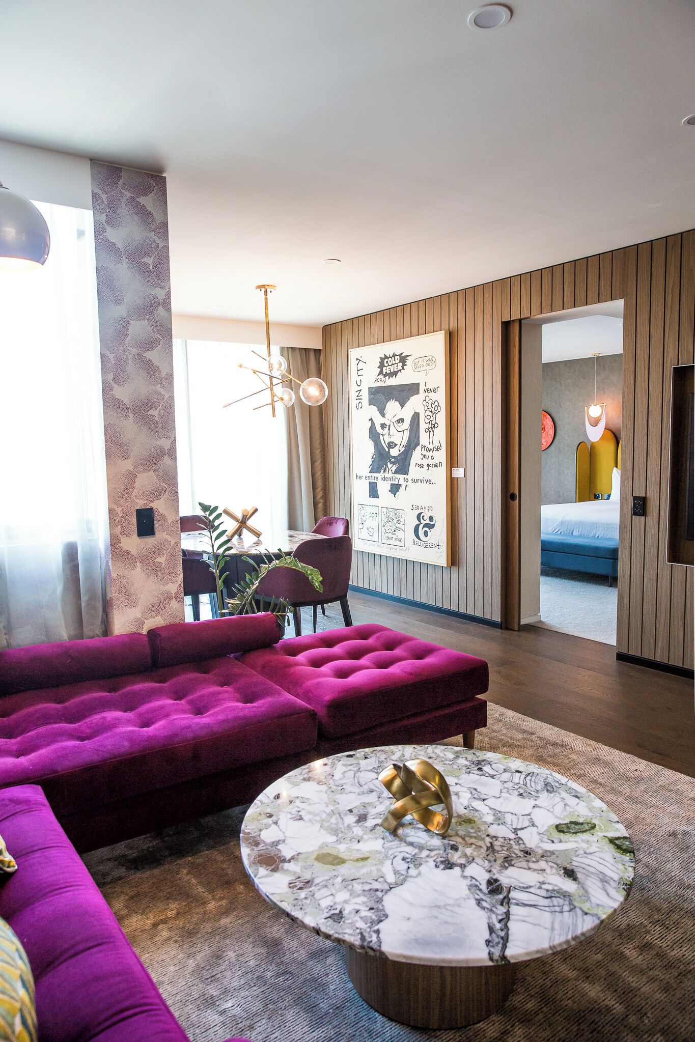 Uma sala de estar moderna com um sofá roxo, uma mesa de centro redonda e uma área de jantar com cadeiras e uma mesa.