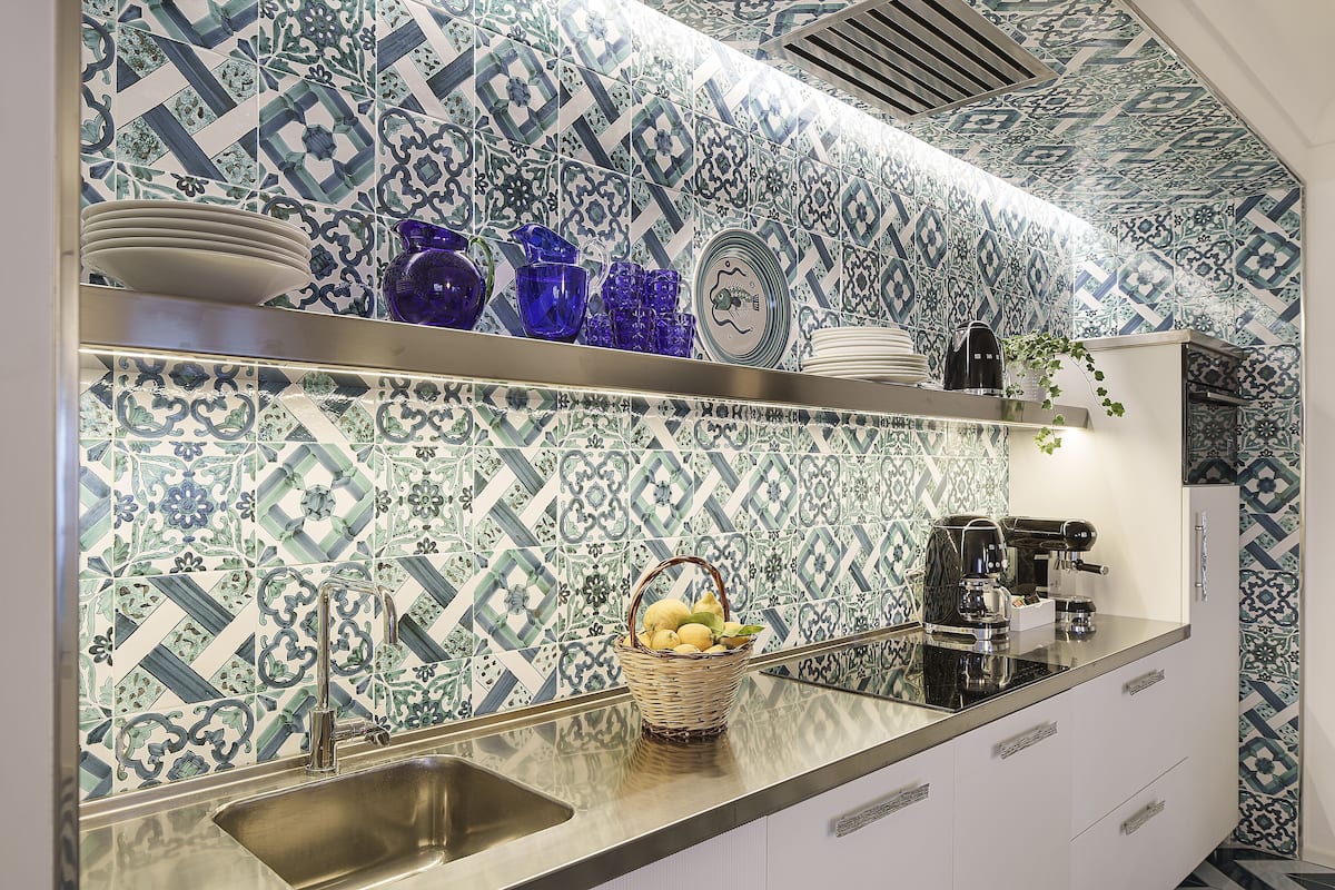 Uma cozinha com painel decorativo atrás do fogão, pia de aço inoxidável e máquina de café.