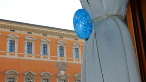 Cortina com detalhe decorativo azul e um edifício com arquitetura clássica ao fundo.