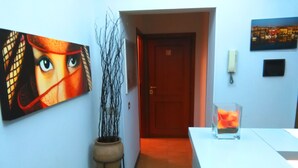 Uma área de recepção com um quadro, um vaso com ramos e um vaso com flores laranjas.