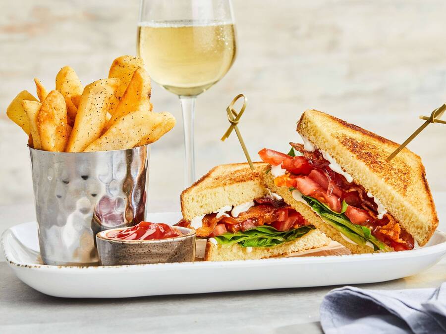 Um prato com um sanduíche grelhado, um copo de vinho branco e um recipiente com batatas fritas.
