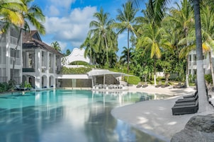Um resort com piscina, palmeiras e área de estar coberta.
