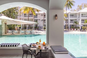 Área de refeições à beira da piscina, com mesa posta para dois, com vista para a piscina e o edifício do resort.