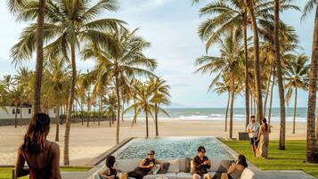 Área à beira da piscina com assentos, palmeiras e vista para a praia.