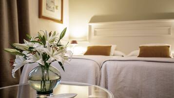 Quarto de hotel com uma cama, uma mesinha de cabeceira com um vaso de flores e um quadro pendurado na parede.