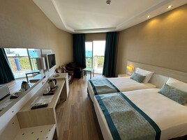 Quarto de hotel com duas camas, uma escrivaninha com televisão e vista para o mar.