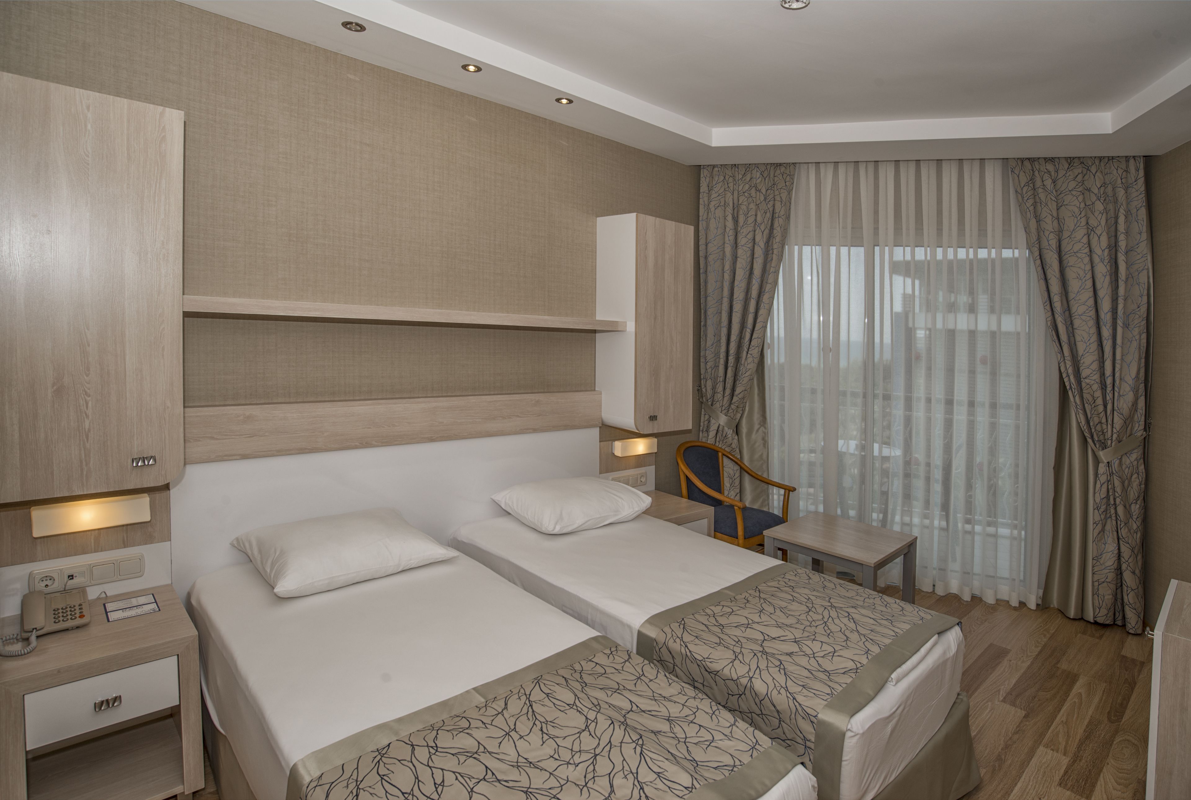 Quarto de hotel com duas camas, uma escrivaninha, uma cadeira, um guarda-roupa e um telefone.