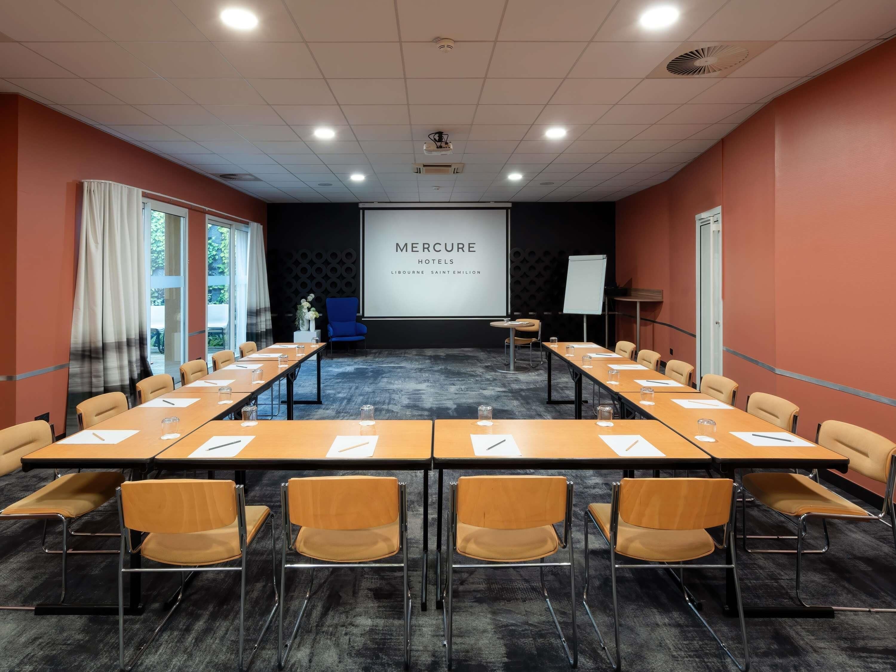 Uma sala de conferência com uma mesa comprida, cadeiras, uma tela de projetor e um quadro branco.