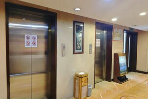 Área de elevador com portas fechadas, um cesto de lixo e um pequeno balcão de informações.