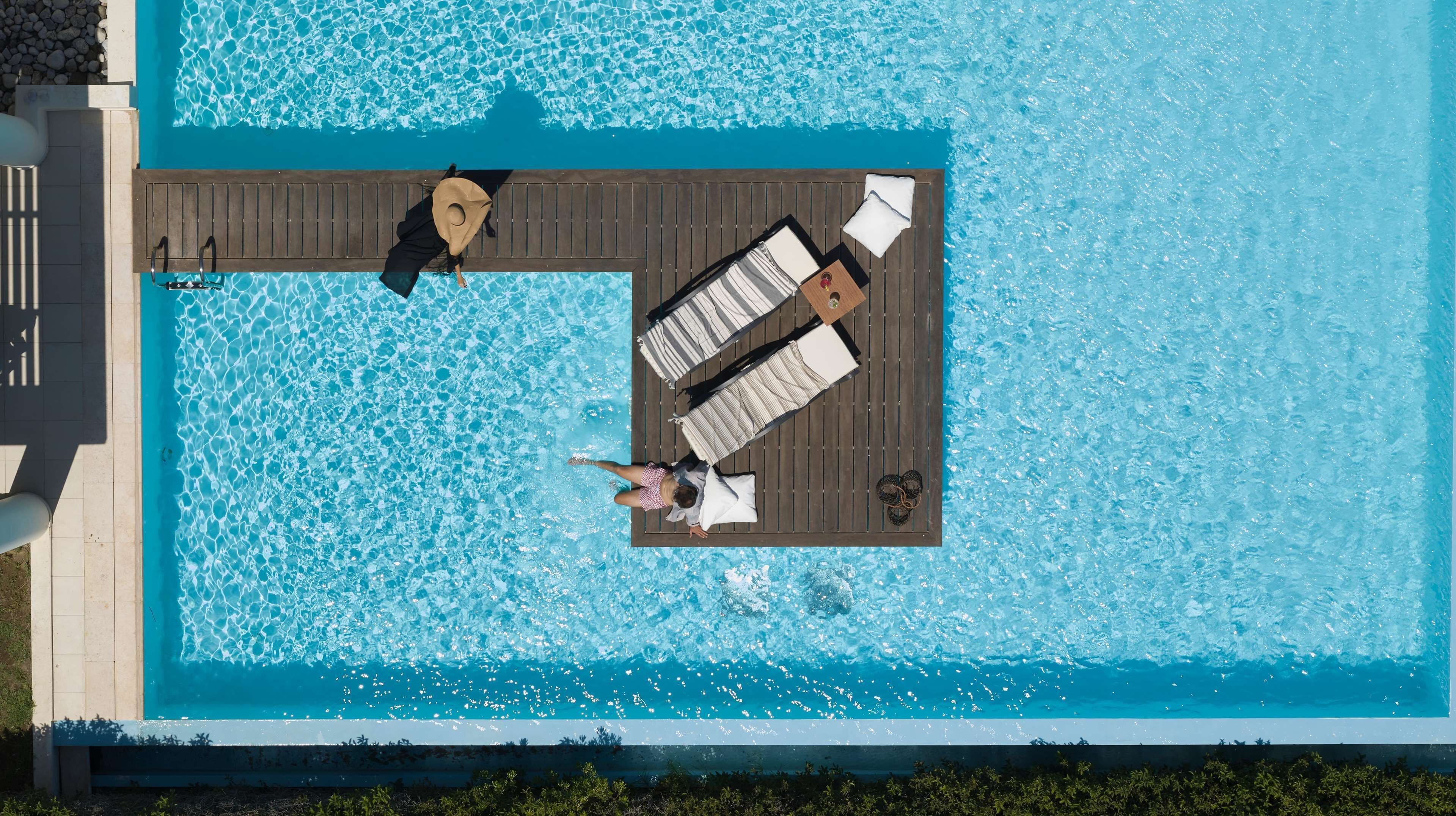 Vista aérea de uma piscina com duas espreguiçadeiras e um deck de madeira.