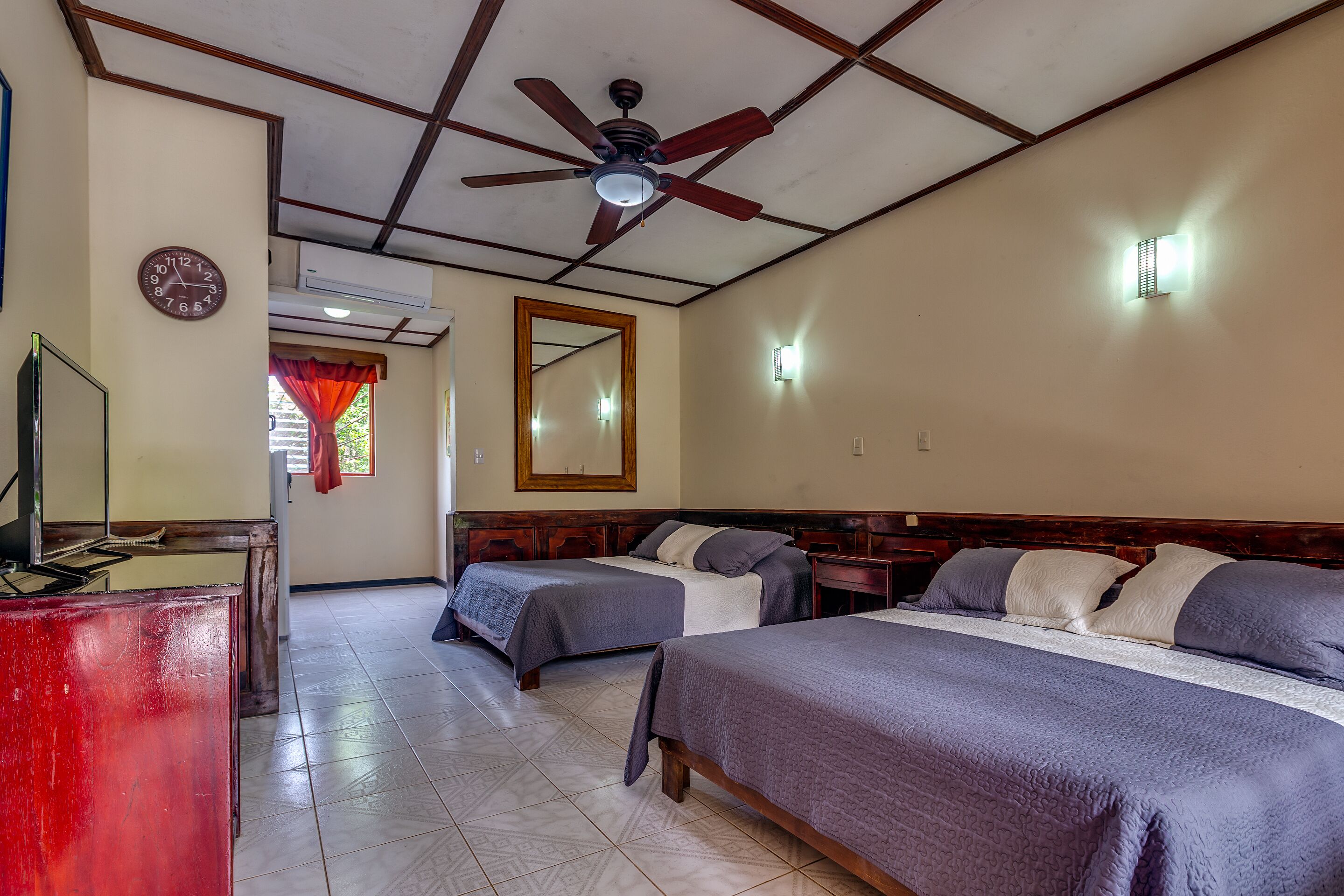Quarto de hotel com duas camas, um ventilador de teto, um relógio e um armário vermelho.