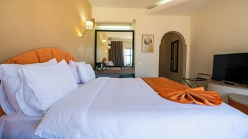 Quarto de hotel com uma cama grande, televisão e banheiro ao fundo.
