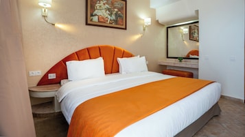 Quarto de hotel com uma cama grande, uma mesa de cabeceira, um espelho e luminárias na parede.