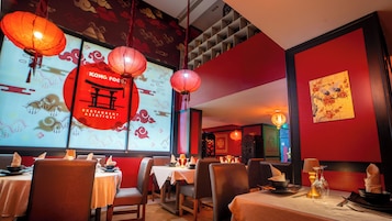 Interior de restaurante com paredes vermelhas, decorações tradicionais chinesas e mesas preparadas para refeições.