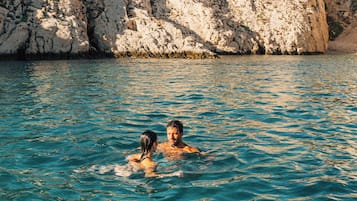 Um casal nada em água azul cristalina, com penhascos rochosos ao fundo.