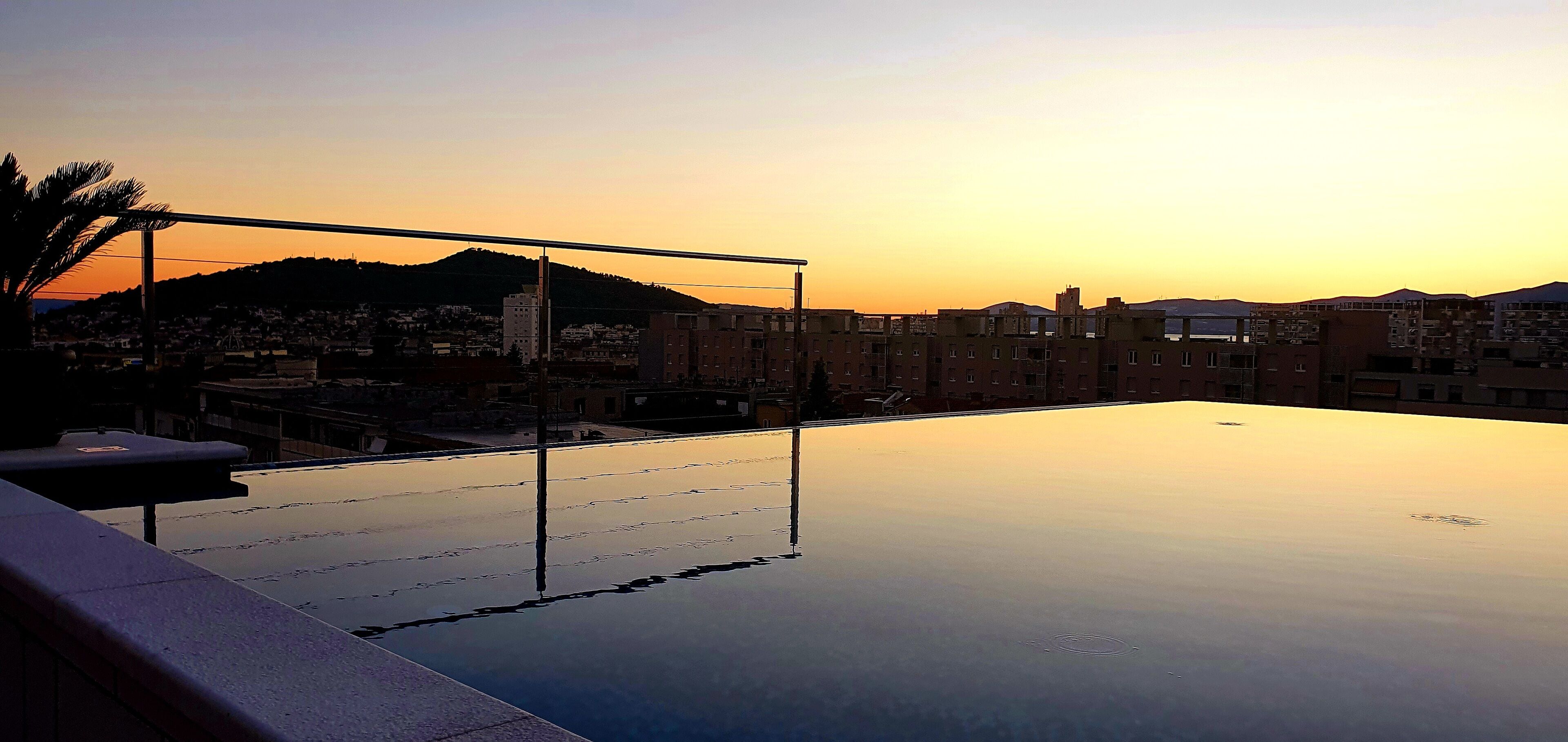 Piscina no terraço com vista para a paisagem urbana ao pôr do sol.