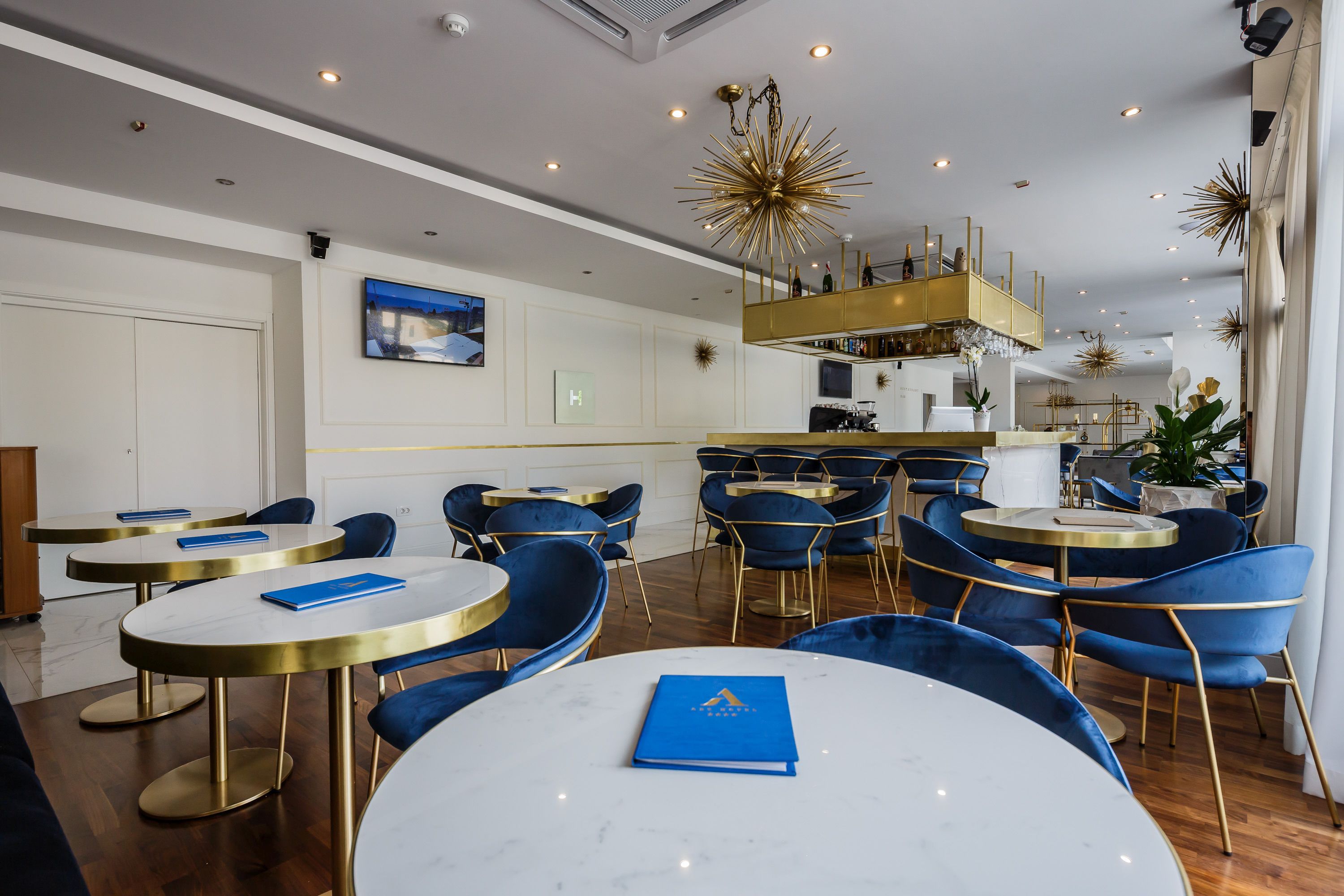 Um interior moderno com mesas redondas e cadeiras azuis, uma área de bar e luminárias decorativas no teto.