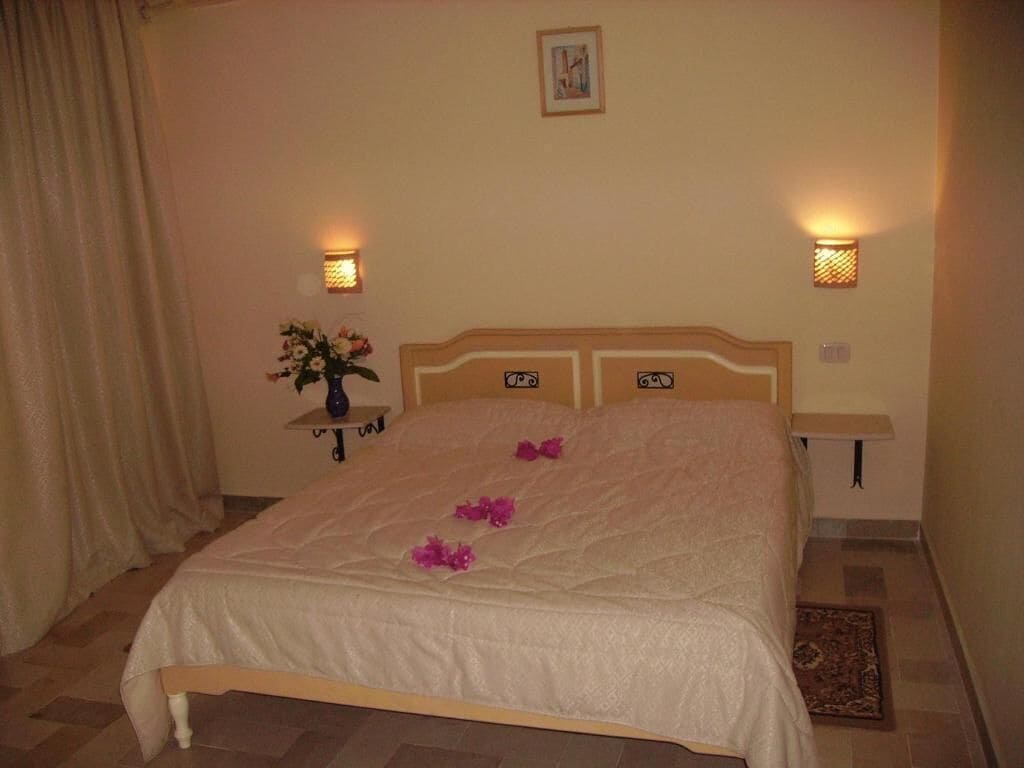 Cama bem arrumada com um arranjo floral e duas luminárias na parede.