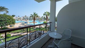Uma varanda com vista para uma área de piscina, incluindo cadeiras de descanso e palmeiras.