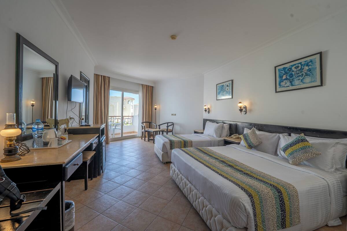 Quarto de hotel com cama, escrivaninha, cadeira, televisão e varanda.