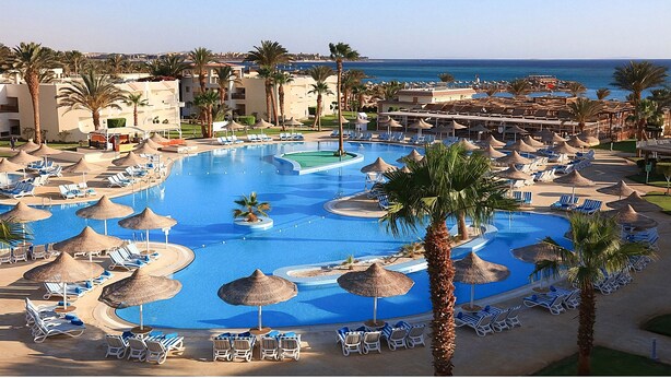 Um resort com uma ampla piscina central, várias piscinas menores e muitos espreguiçadeiras e guarda-sóis.