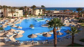 Um resort com uma ampla piscina central, várias piscinas menores e muitos espreguiçadeiras e guarda-sóis.