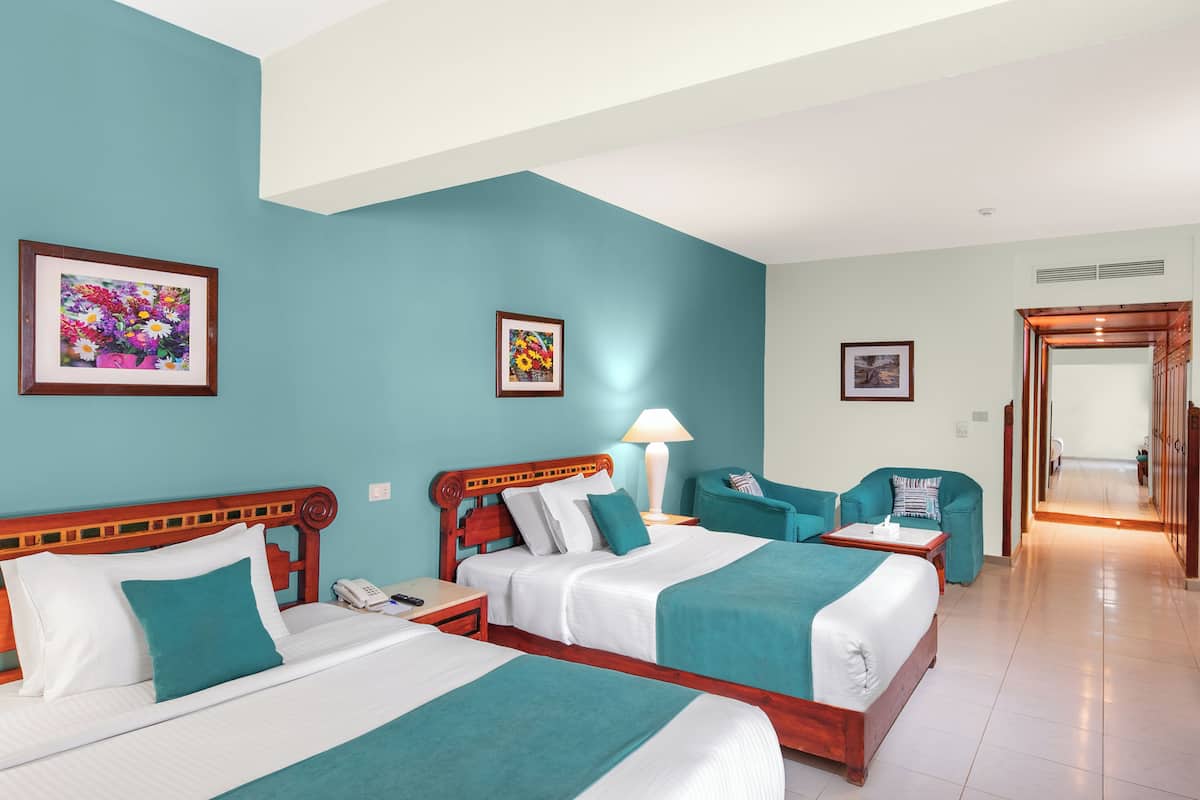 Quarto de hotel com duas camas, paredes verde-água e cabeceira de madeira.