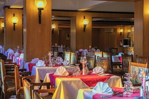 Restaurante com várias mesas preparadas para refeições, cadeiras de madeira e luminárias fixadas na parede.