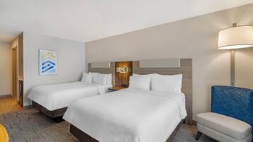 Quarto de hotel com duas camas, uma cadeira, um abajur e uma obra de arte na parede.